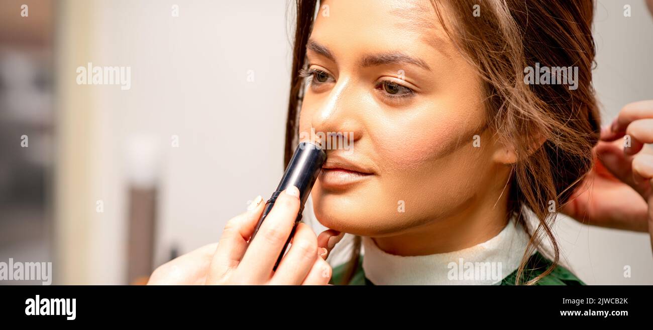 Beautiful young brunette woman receiving makeup with stick concealer on ...