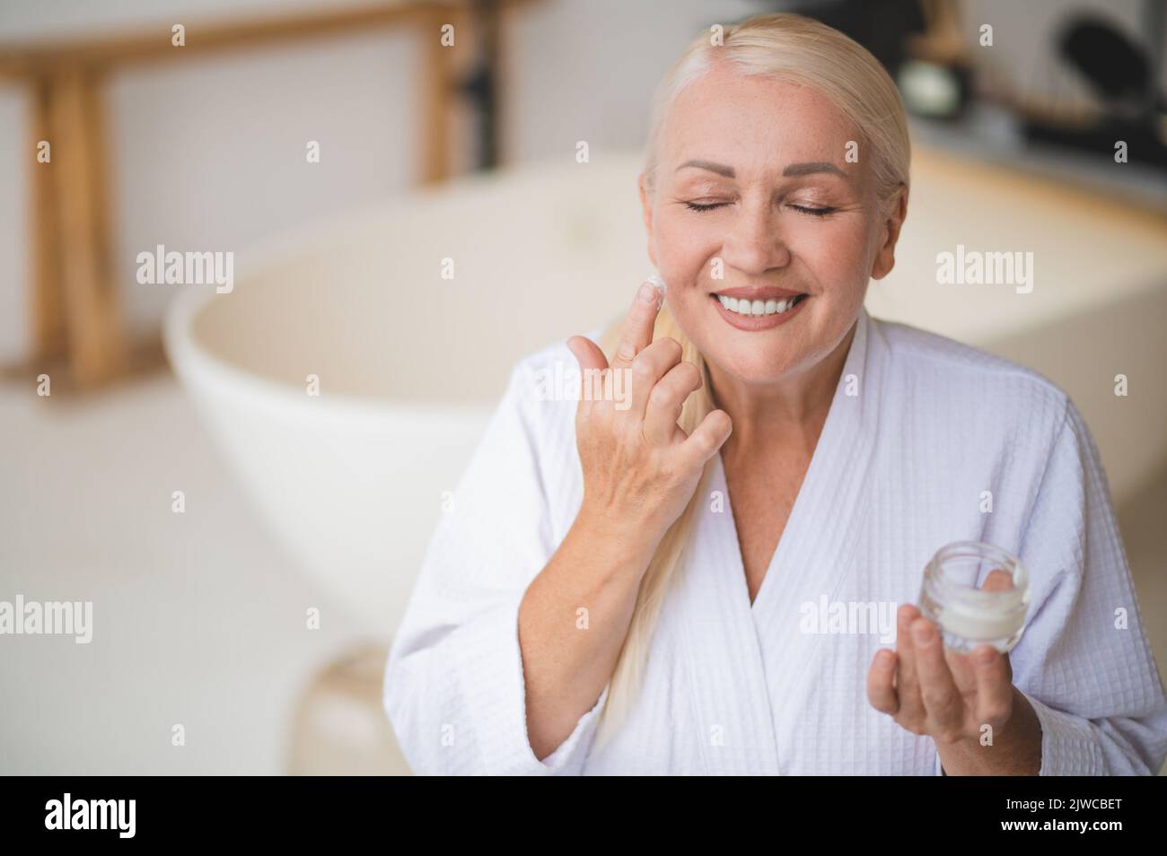 Pretty well-groomed woman applying cream on her face Stock Photo - Alamy