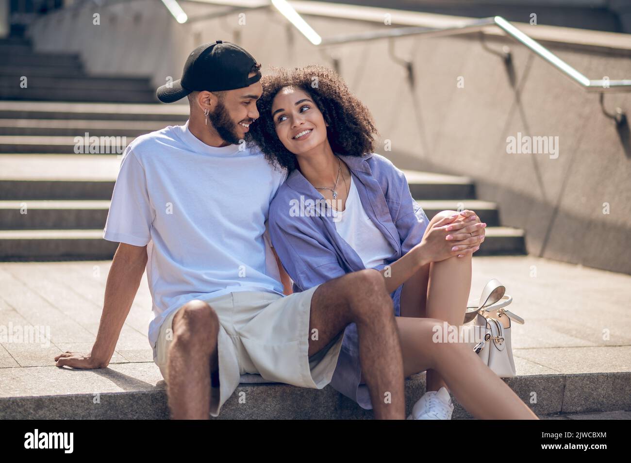 Young cute couple sitting on the steps and looking peaceful and happy ...