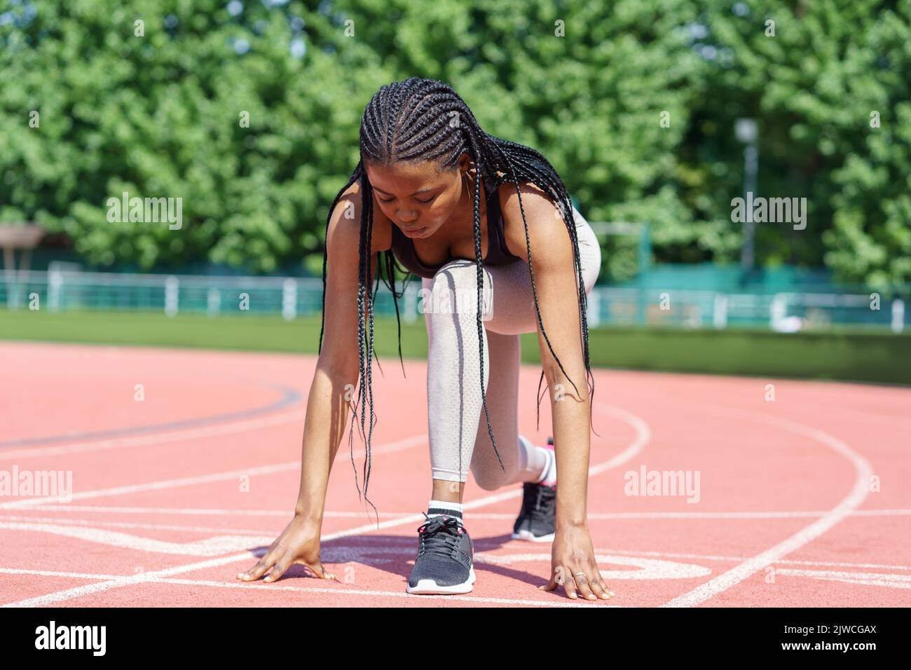 African American woman with long braids prepares low start running ...