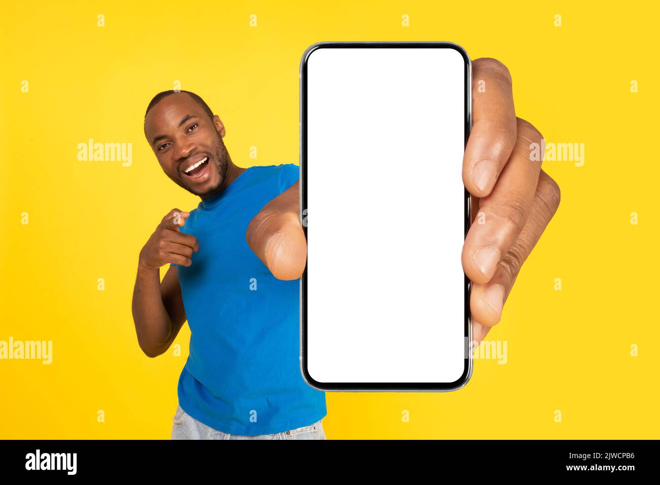 Joyful Black Guy Holding Phone With Large Screen, Yellow Background ...