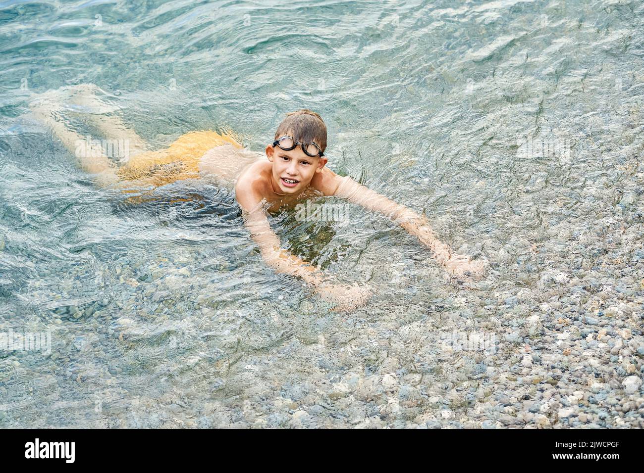 Schoolboy enjoys swimming in shallow sea water with pebble bottom ...
