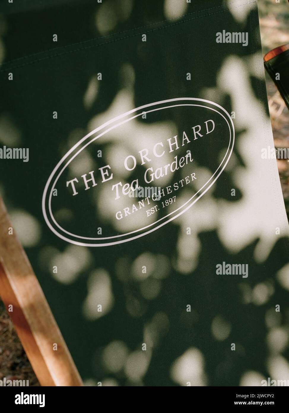 The Orchard Tea Gardens outdoor seating with logo and dappled light in ...
