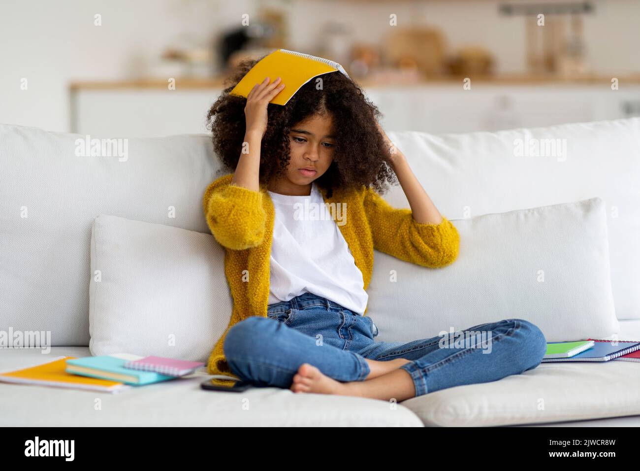 Tired african american school girl doing homework, sitting on couch ...