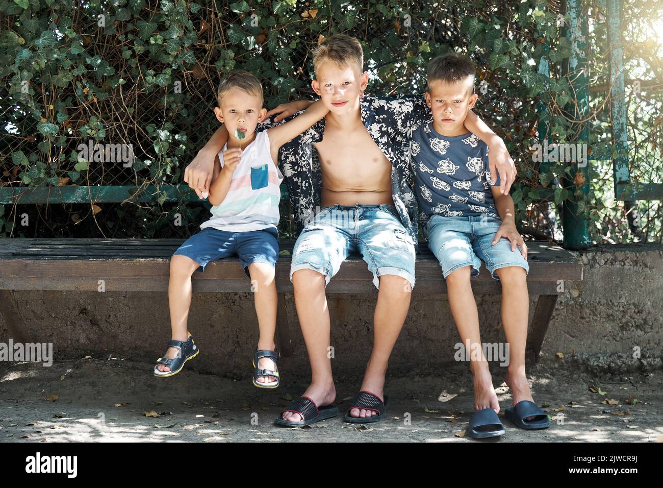 Friendly siblings sit on stone bench resting in tree shadow on summer ...