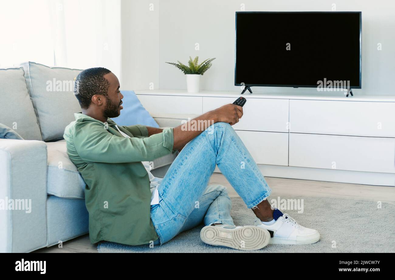 African american man watching television, pointing remote control at ...