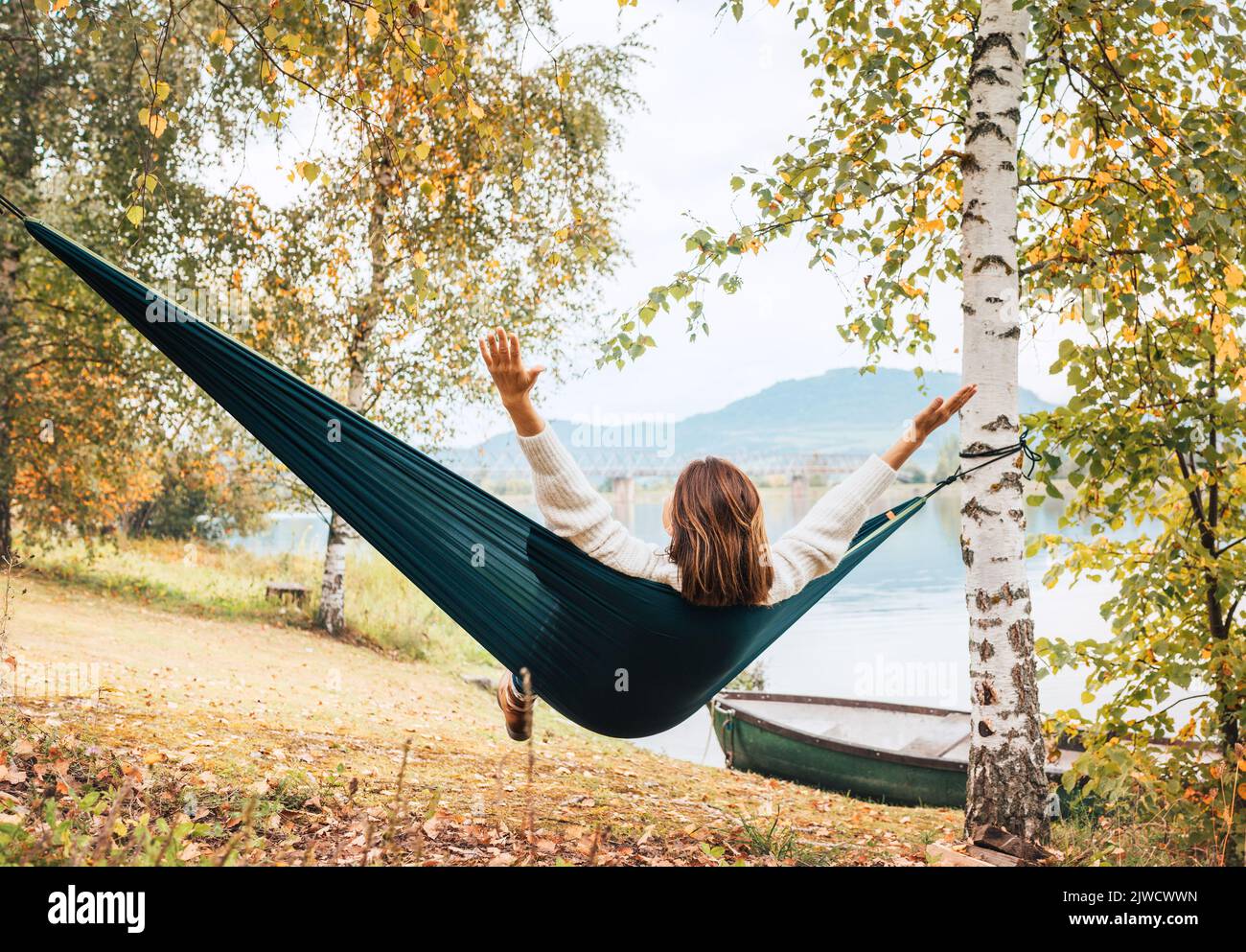 The young woman cheerfully rose arms up while she swinging in a hammock ...