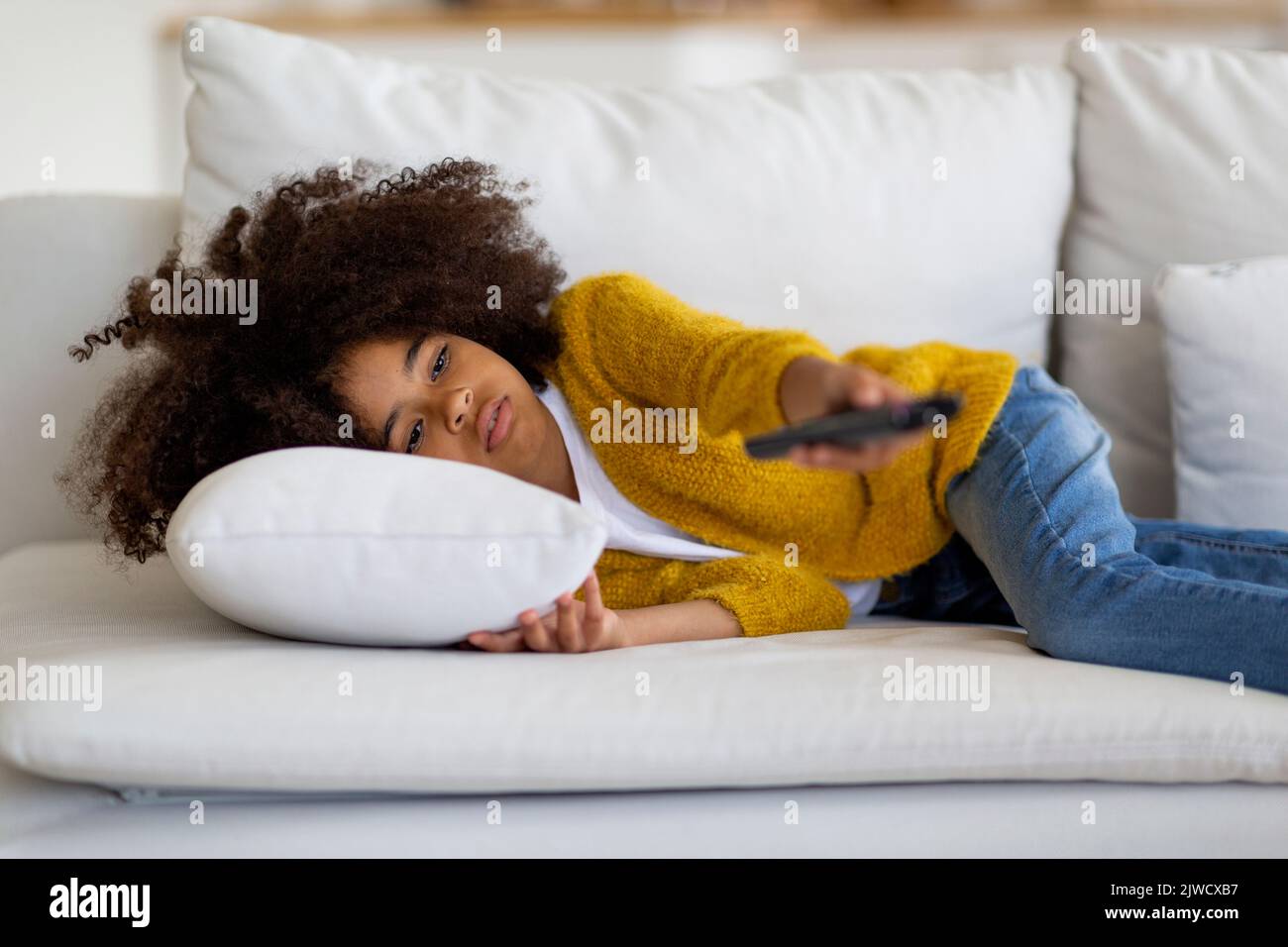 Bored black school girl lying on couch, watching TV Stock Photo - Alamy