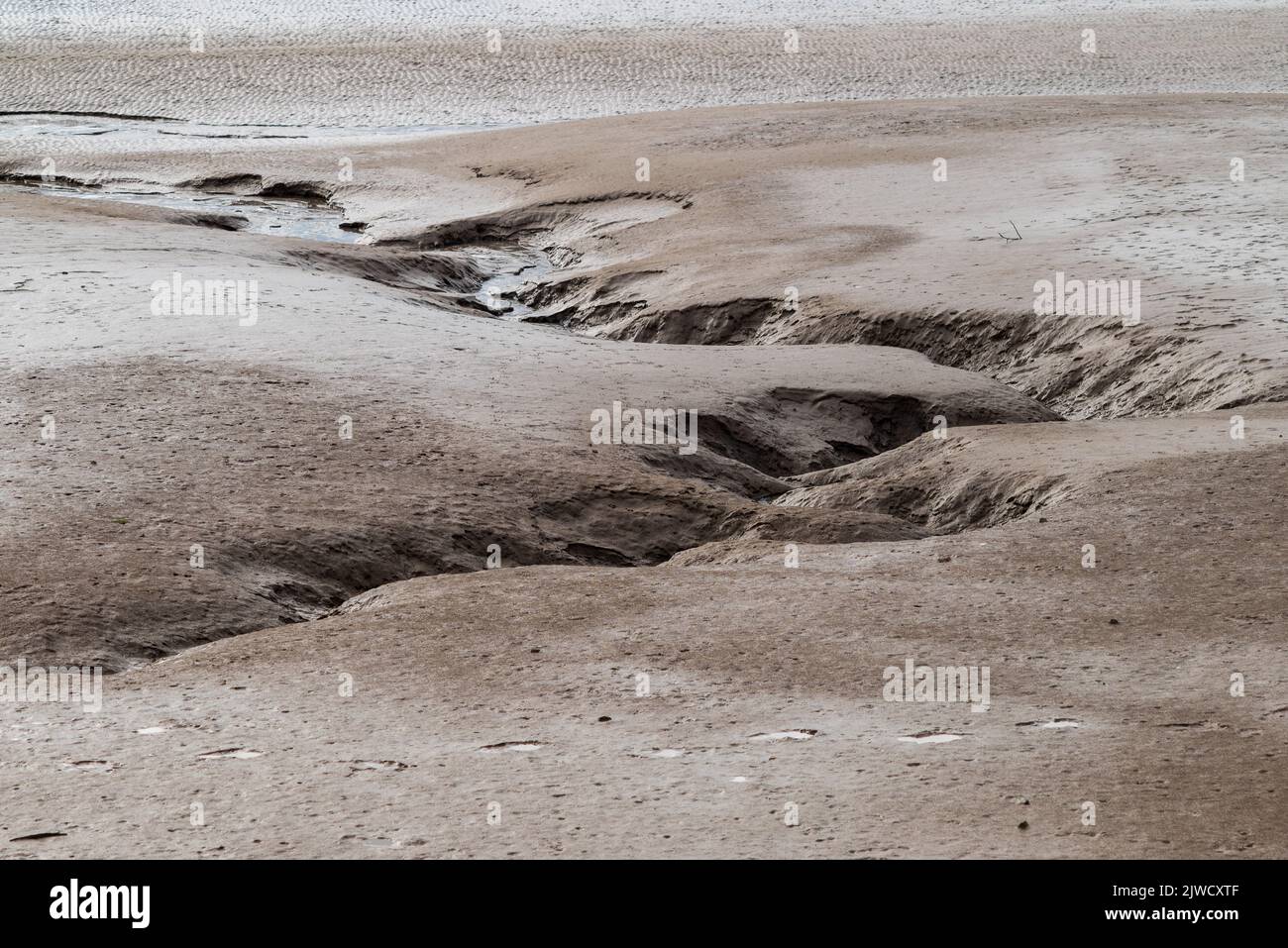 Water channel winding through mud and quicksand left by low tide over ...