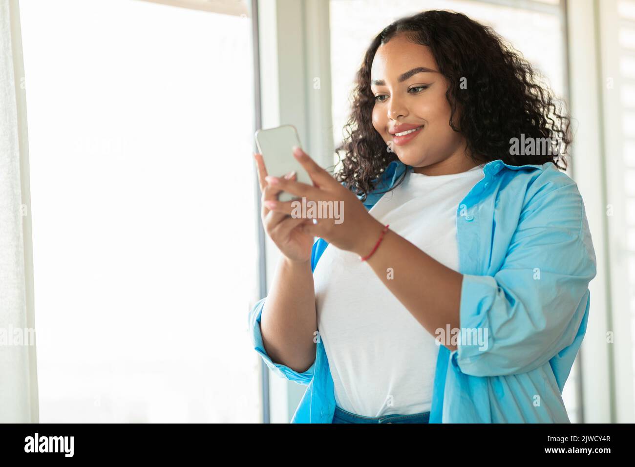 Happy Plump Black Lady Using Phone Texting Standing At Home Stock Photo ...