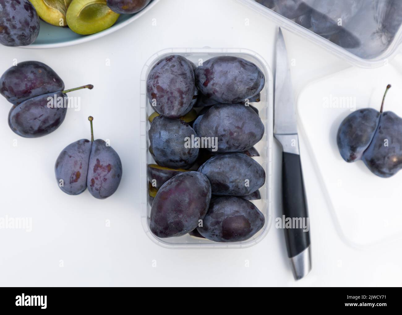 Whole and halves of a blue plums lie on a plate and in open plastic box ...