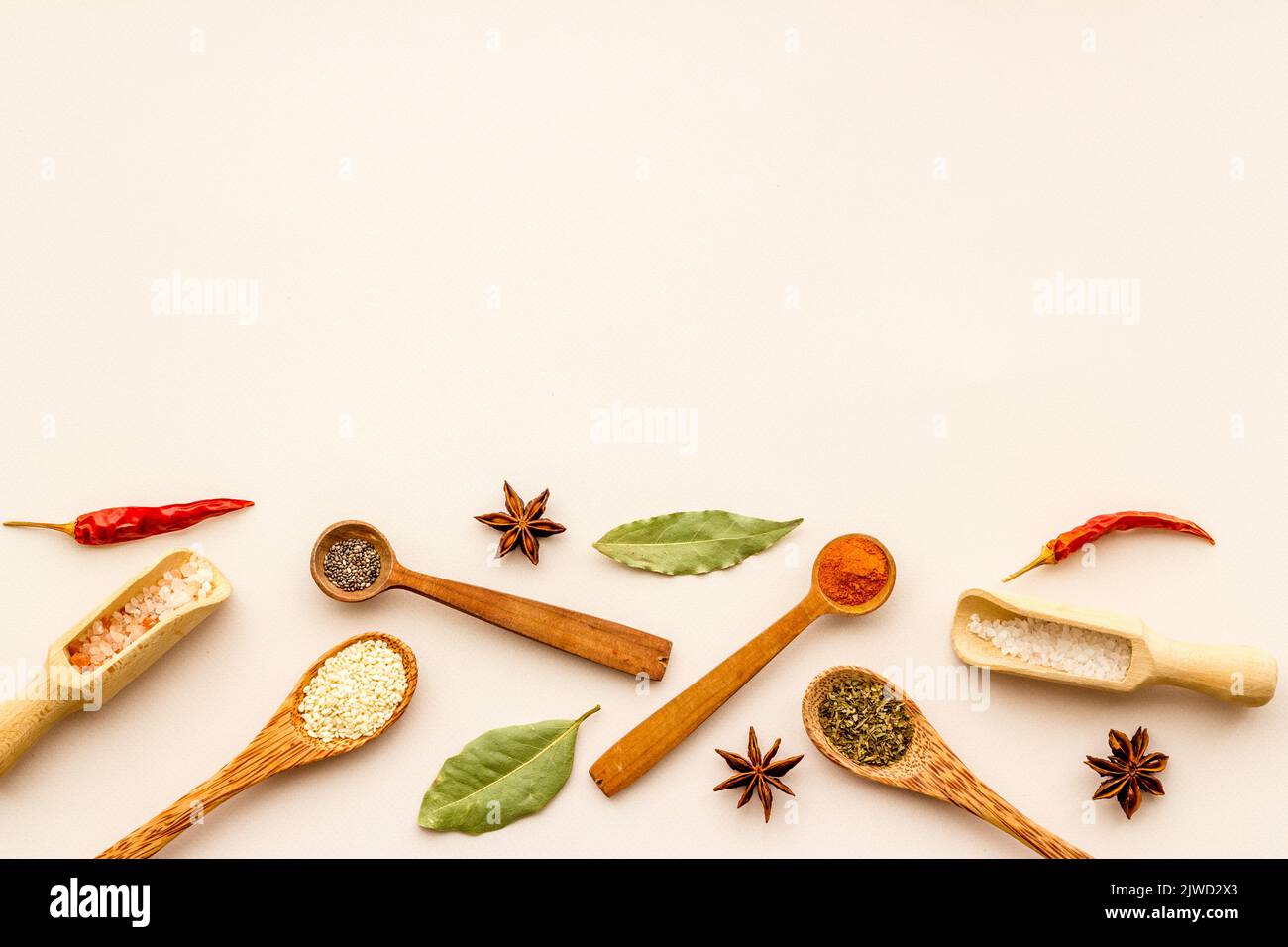 Variety of colorful spices and herbs in wooden spoons on kitchen table ...