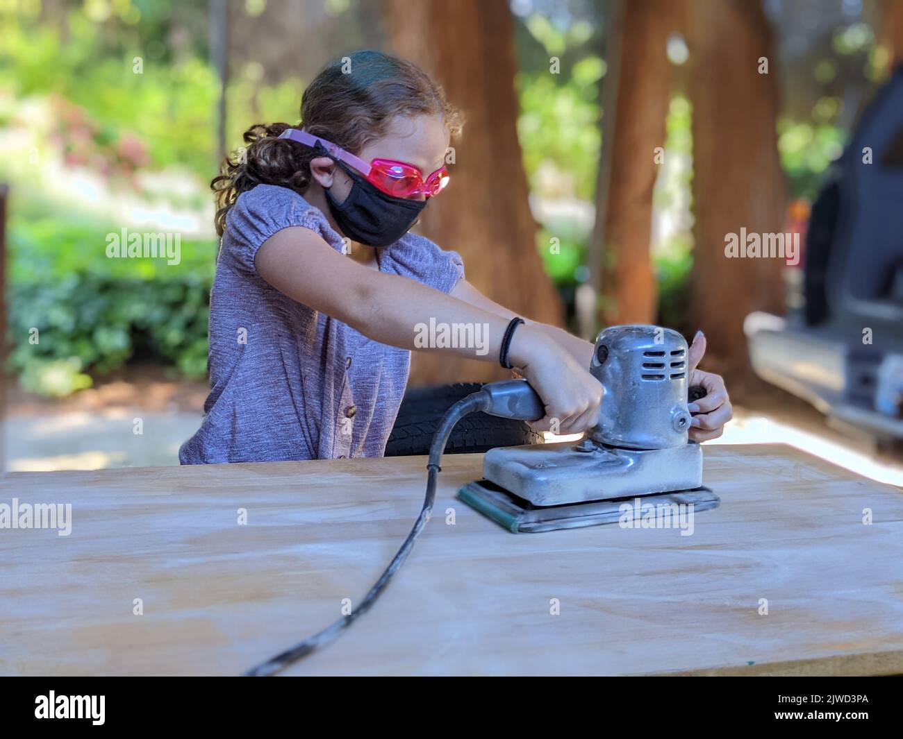A girl working with an electric jigsaw cutting wood with saw ...