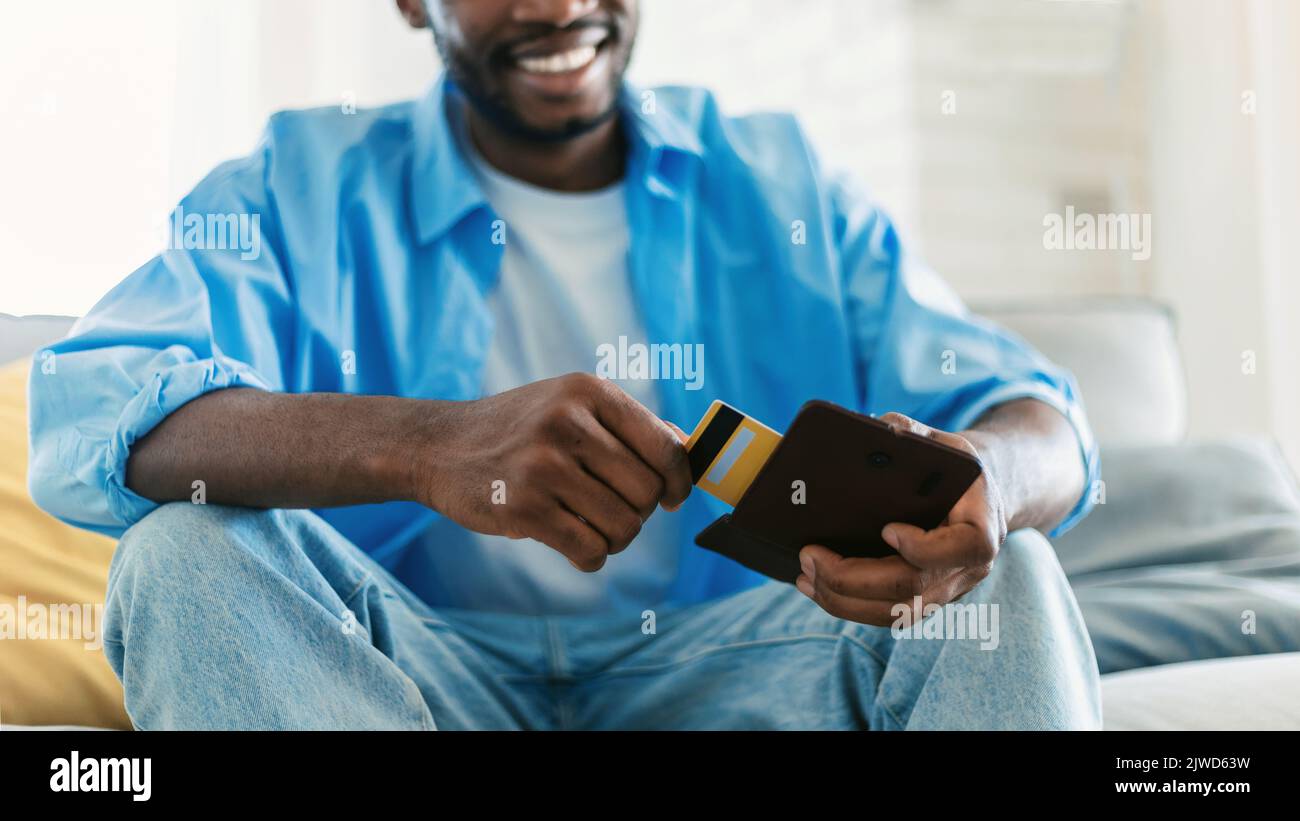Happy african american man taking credit card out of wallet, sitting on ...