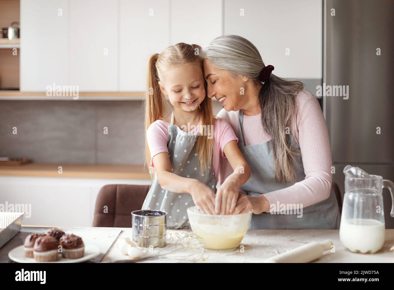 Satisfied old female in apron hugs little granddaughter, make dough ...