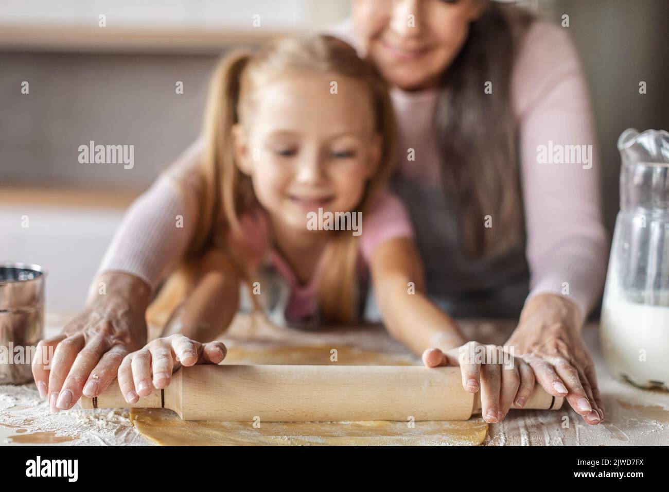 Smiling european granddaughter and elderly grandma in aprons make dough ...