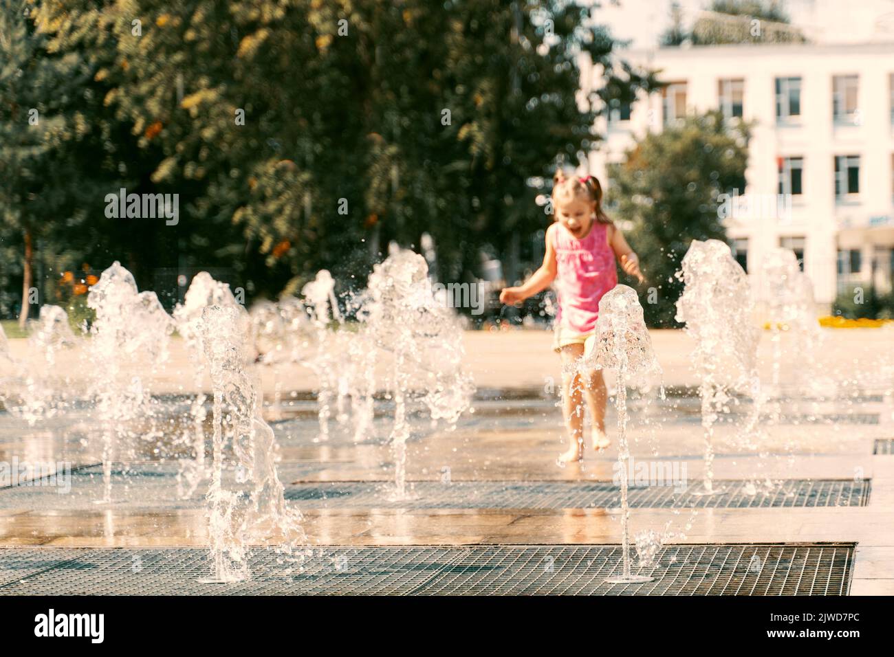 little girl playing with small fountains on the urban plaza. focus on ...