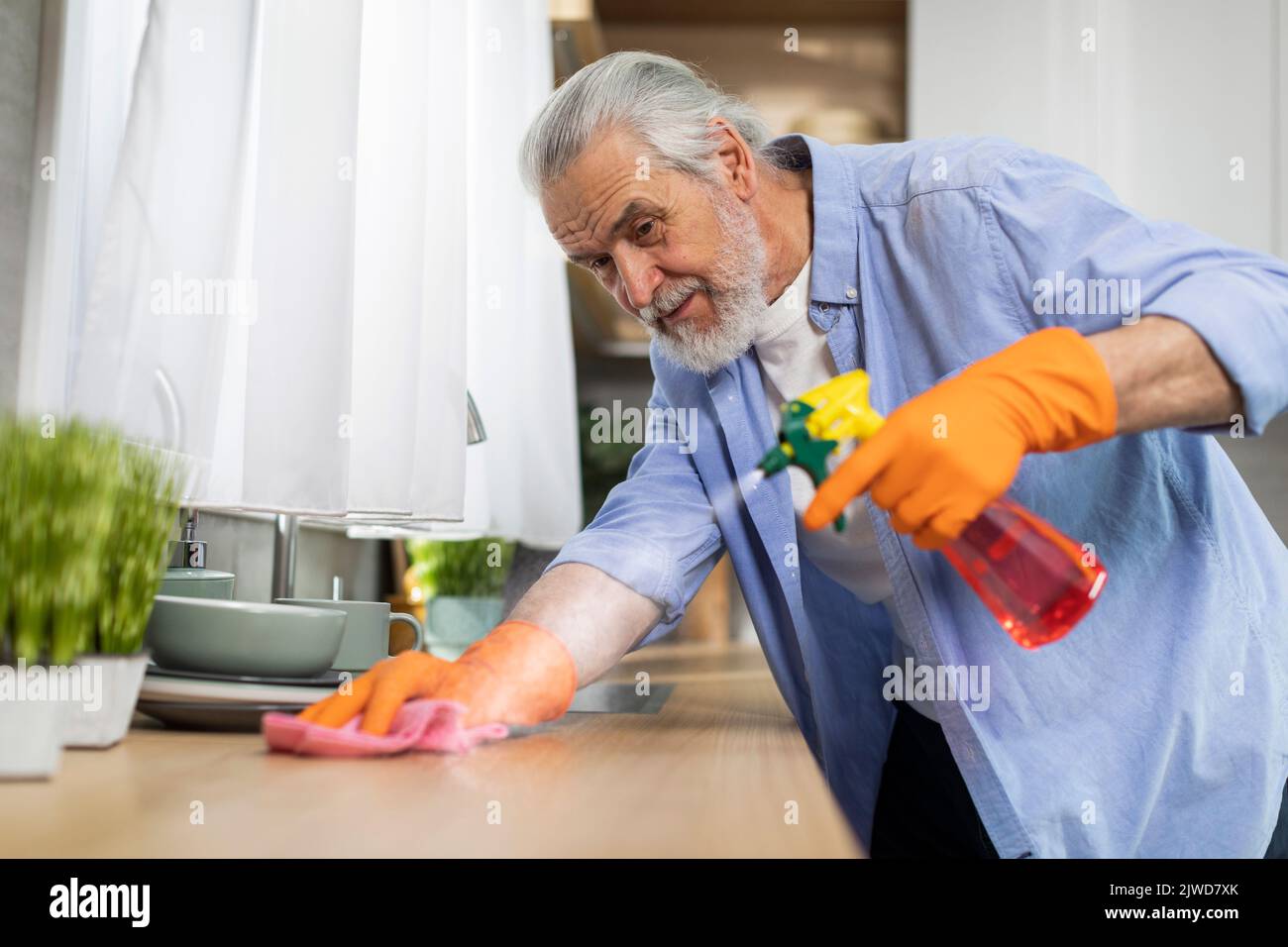 Portrait Of Smiling Senior Man Cleaning Table In Kitchen From Dust ...