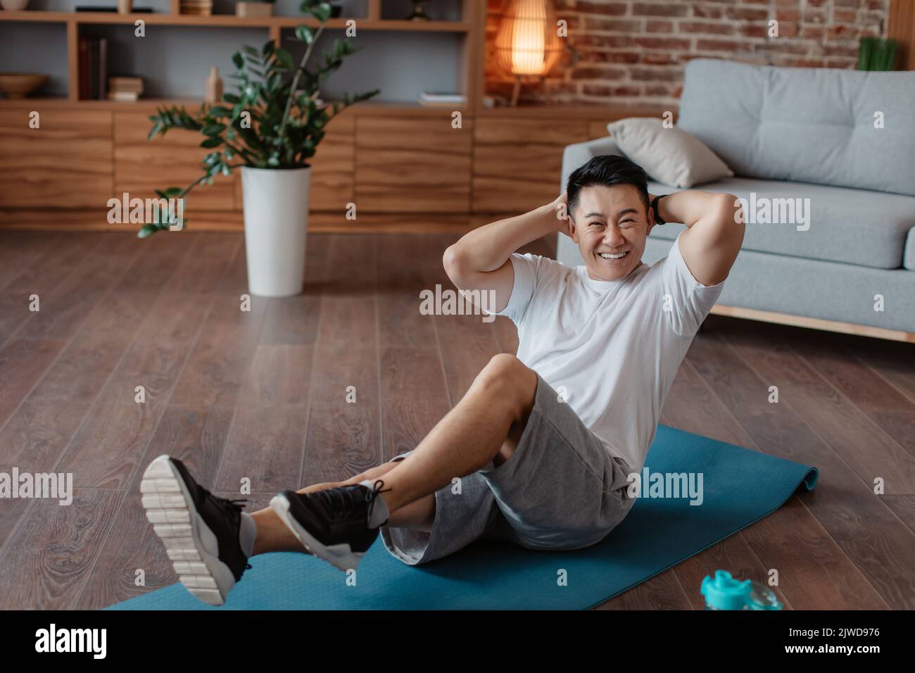 Happy asian man doing abs exercises, working out at home on fitness mat ...