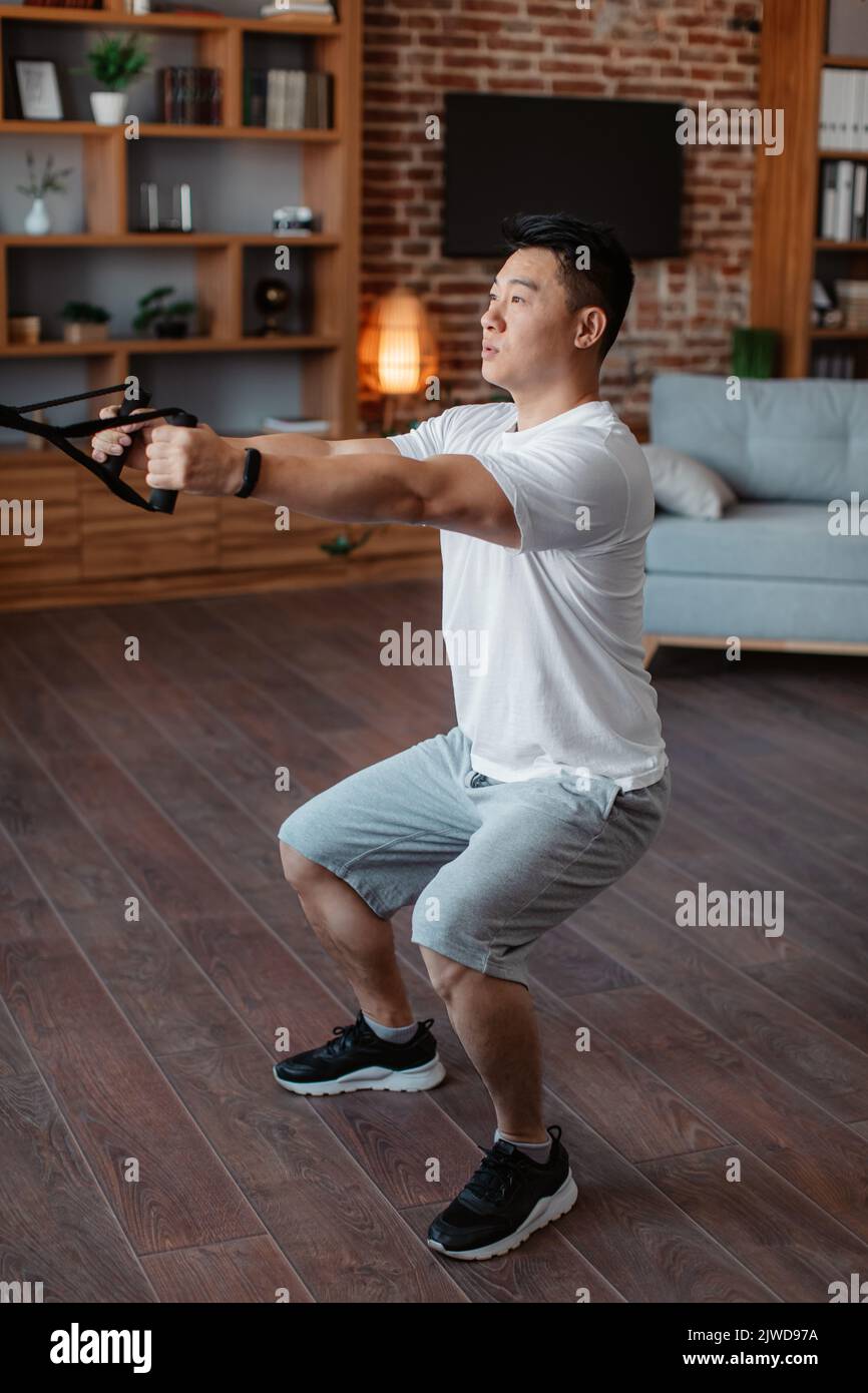 Mature asian man working out with resistance band, doing squats ...