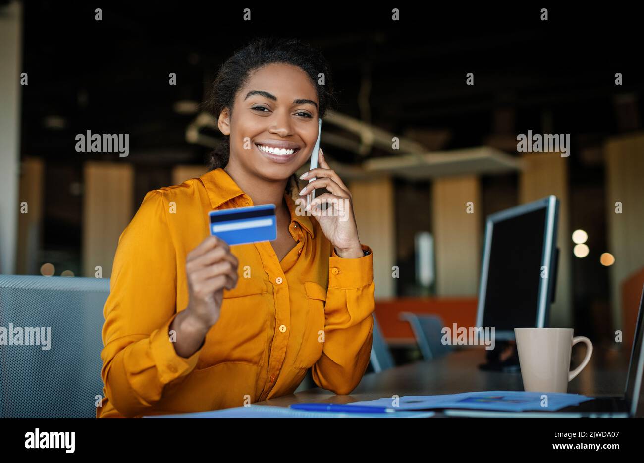 Easy payments concept. Happy black female worker holding credit card after online purchase and ...