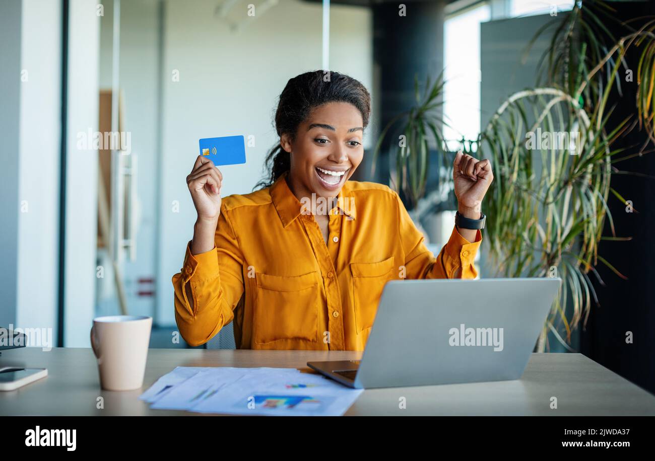Overjoyed black female office worker holding credit card in front of ...