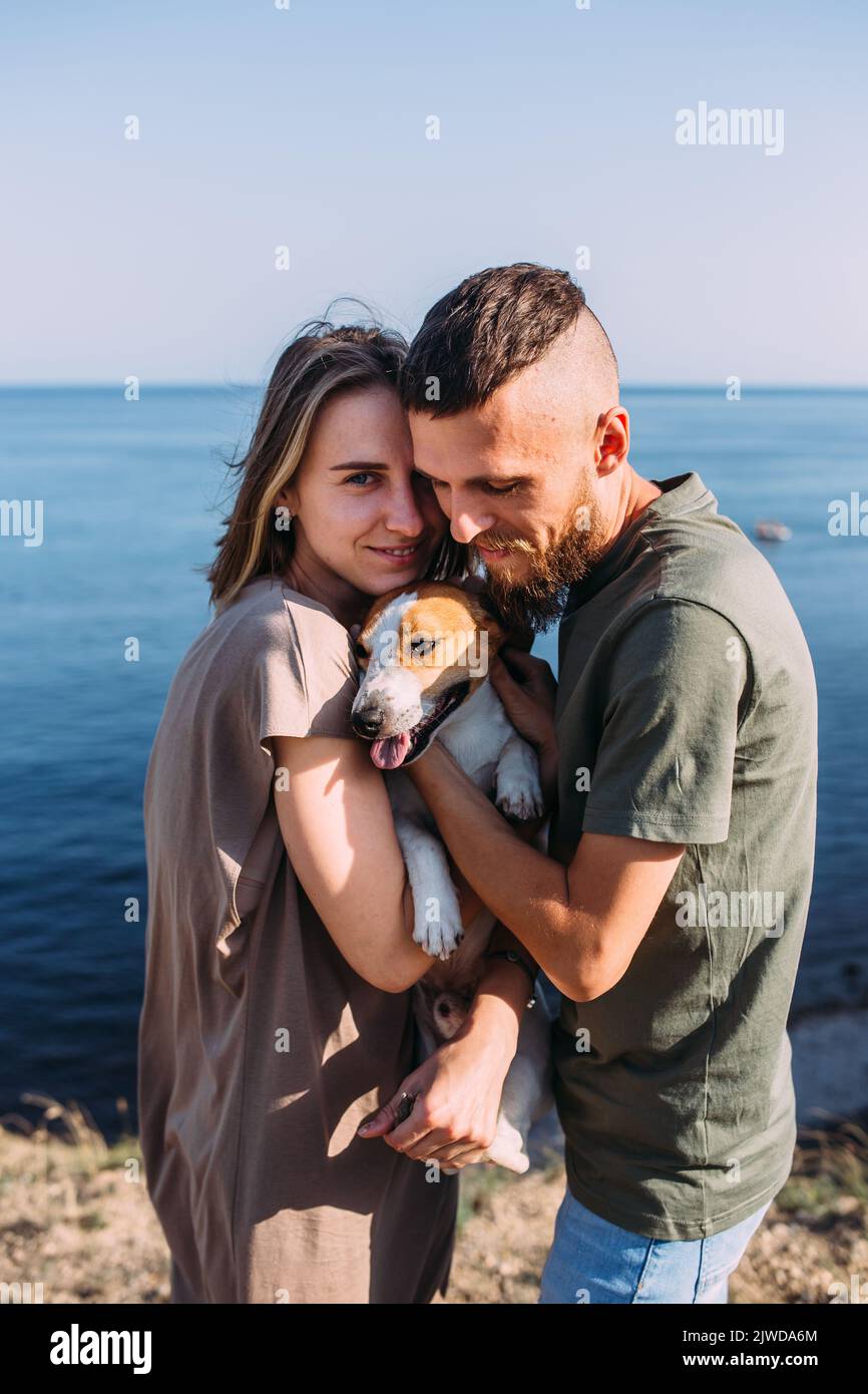 Happy couple with favourite pet. Young man and woman have walk near sea ...