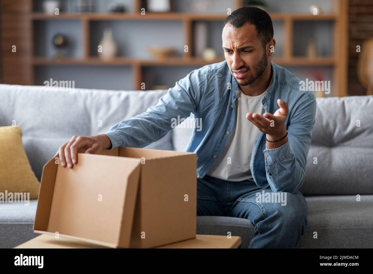 Wrong Parcel. Confused black man looking at open cardboard box at home ...
