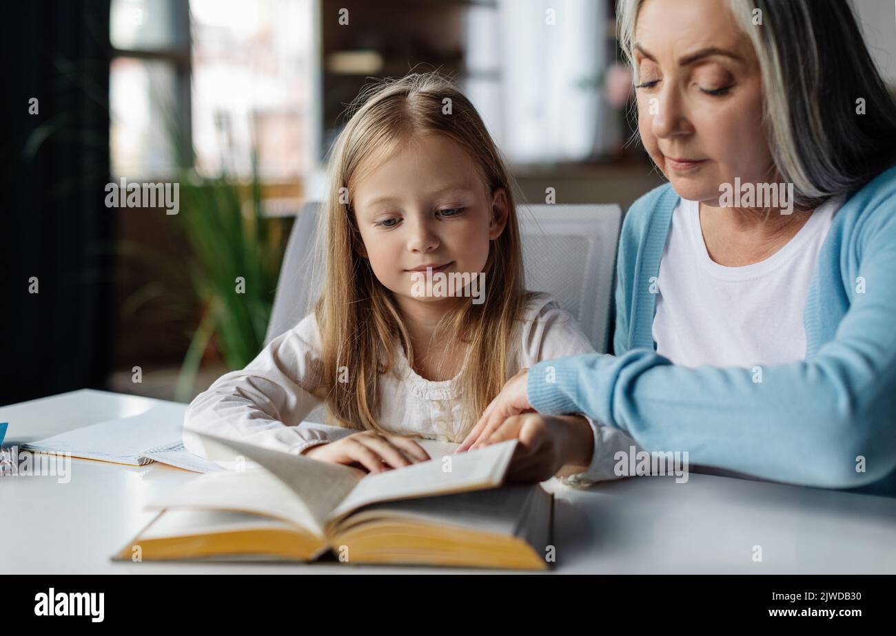 Concentrated european little girl and mature woman reading book on ...