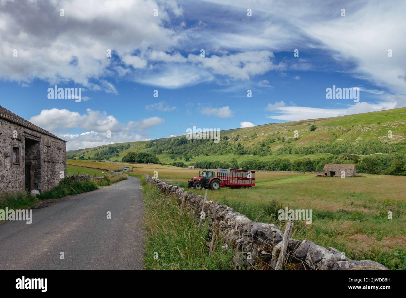 Farmer driving a tractor pulling a livestock trailer out of a field ...