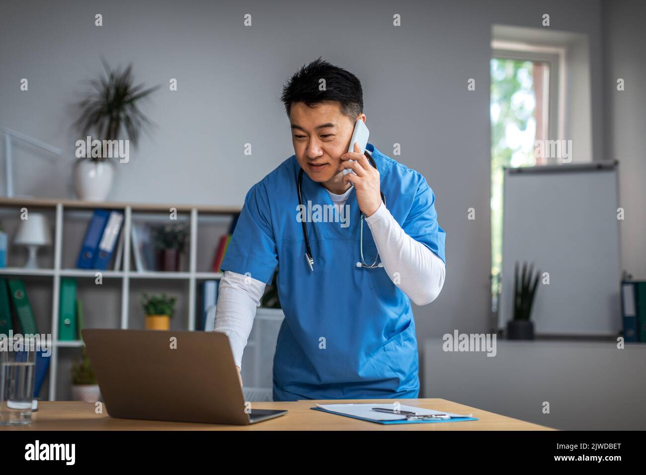 Serious millennial chinese male doctor calling by phone and looking at ...