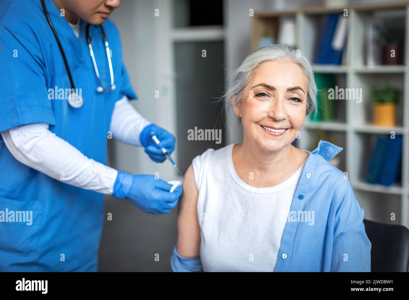 Millennial man doctor make injection to smiling elderly lady patient in ...