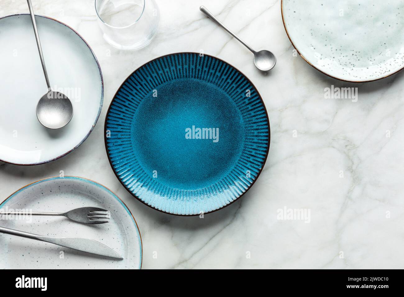 Modern tableware set with cutlery, a glass, and a vibrant blue plate, overhead flat lay shot ...