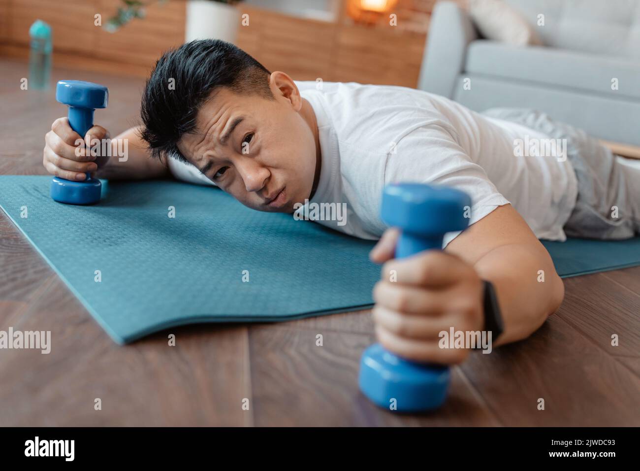 Exhausted asian mature man laying down on yoga mat with dumbbells in ...