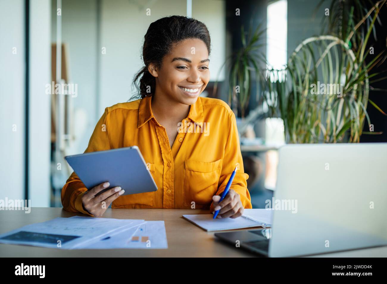 Positive black woman using digital tablet and laptop, working online in ...