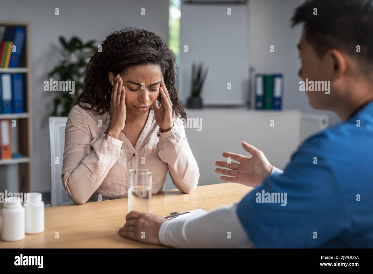 Serious adult asian male doctor calms sad young african american female ...