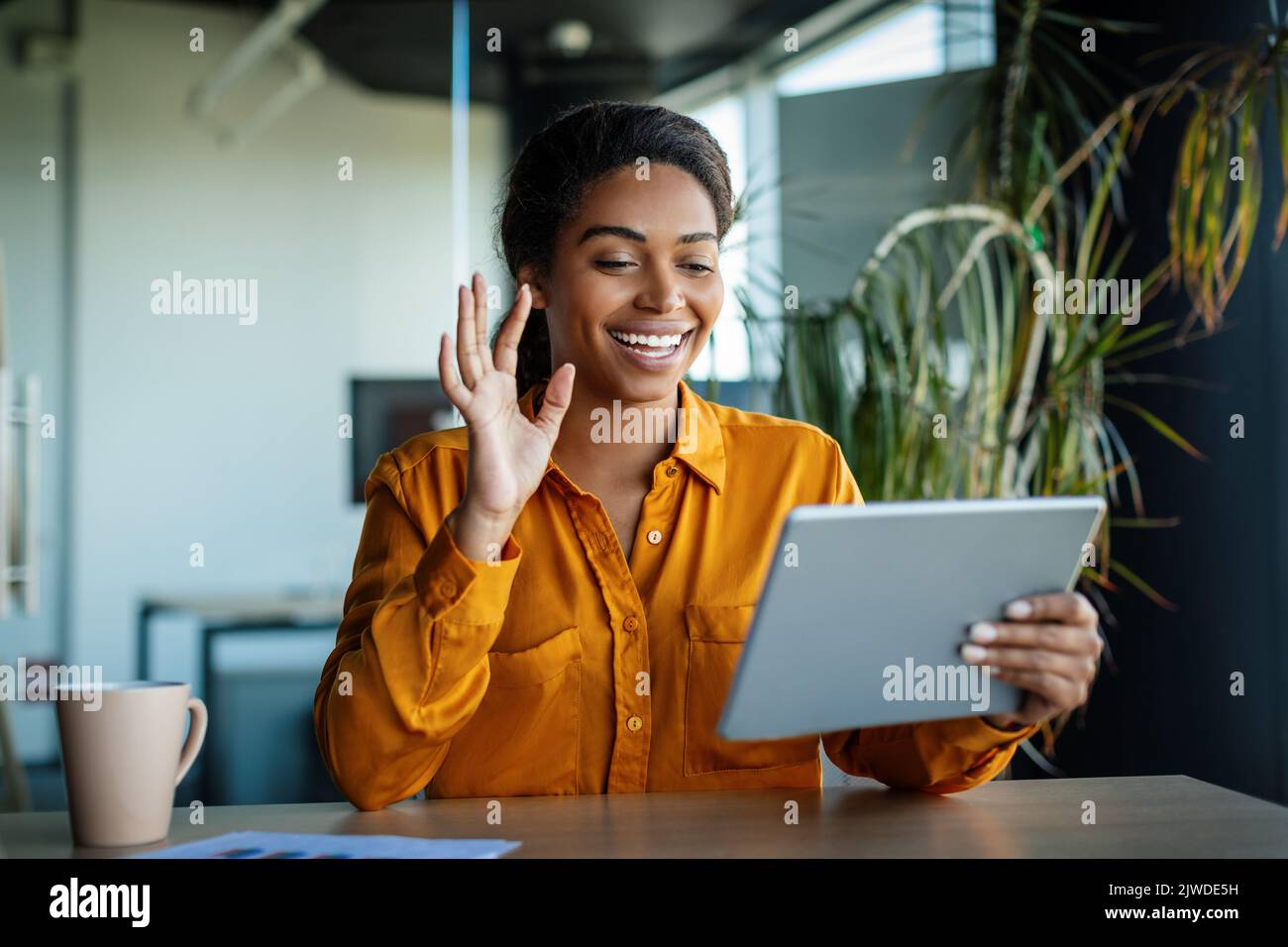 Happy black businesswoman sitting at table in office, having video chat ...