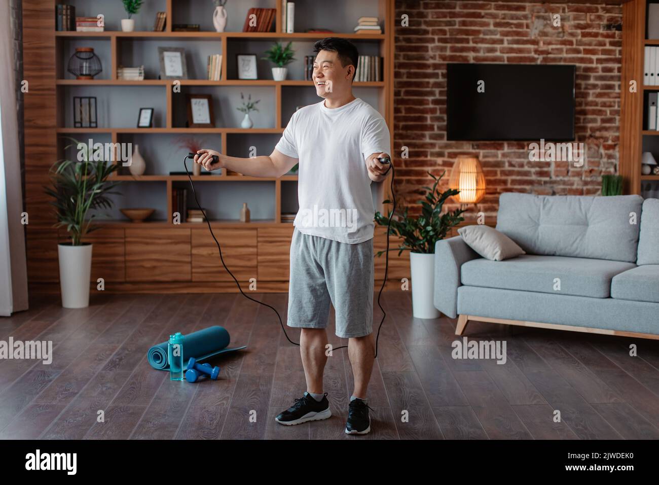 Sporty asian mature sportsman with jumping rope exercising at home ...