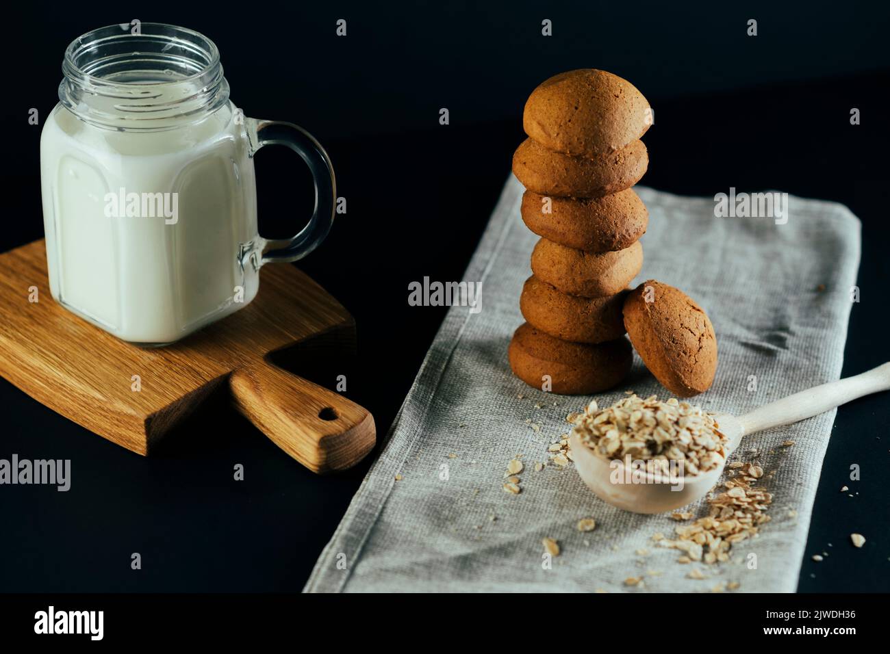 Stack of fresh oatmeal cookies with milk in jar, raw oat flakes in ...