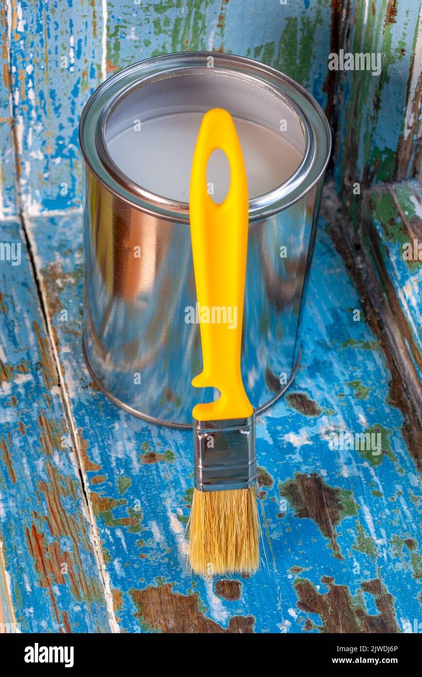 an open can of white paint and a yellow brush on a wooden windowsill ...