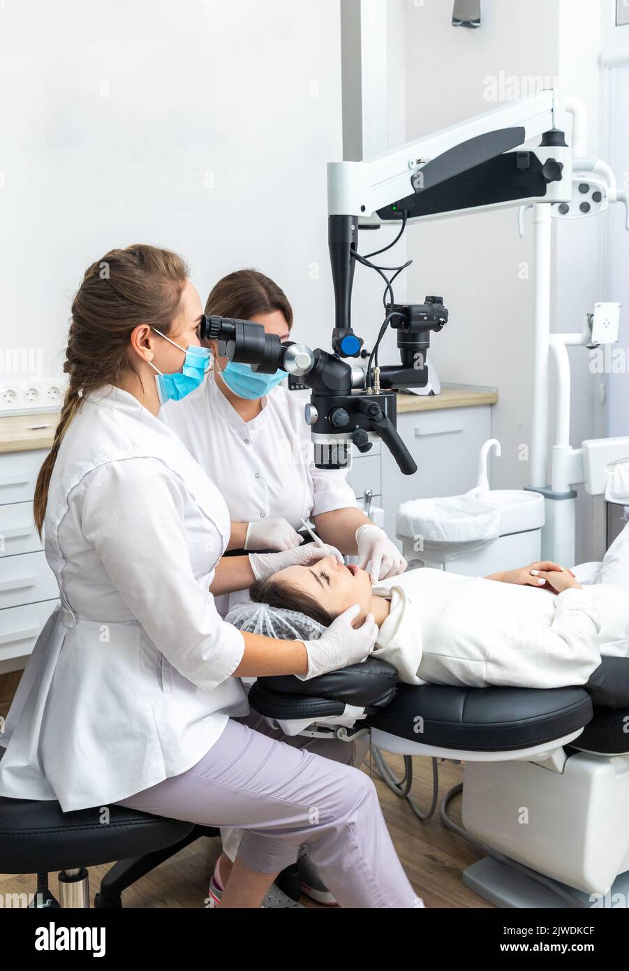 Female dentist using dental microscope treating patient teeth at dental ...