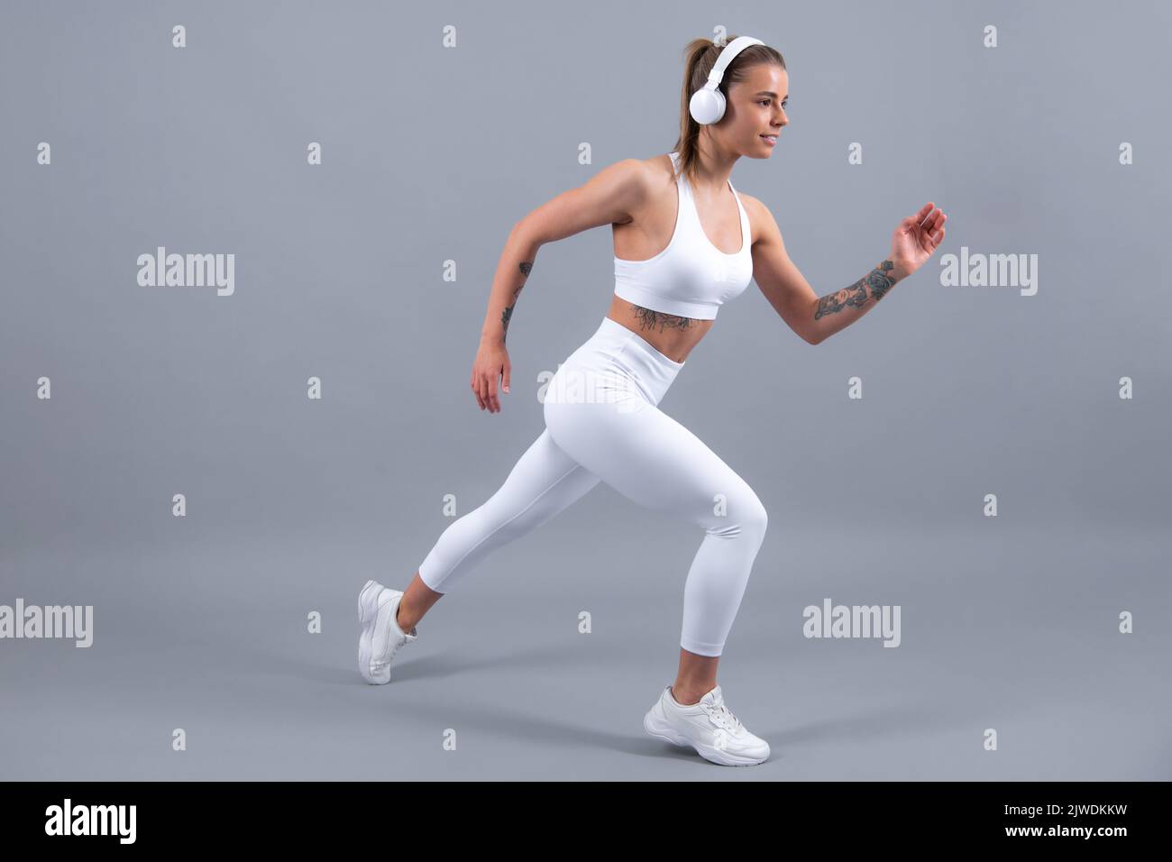 Fitness woman runner. Sporty strong cheerful young woman posing on gray ...