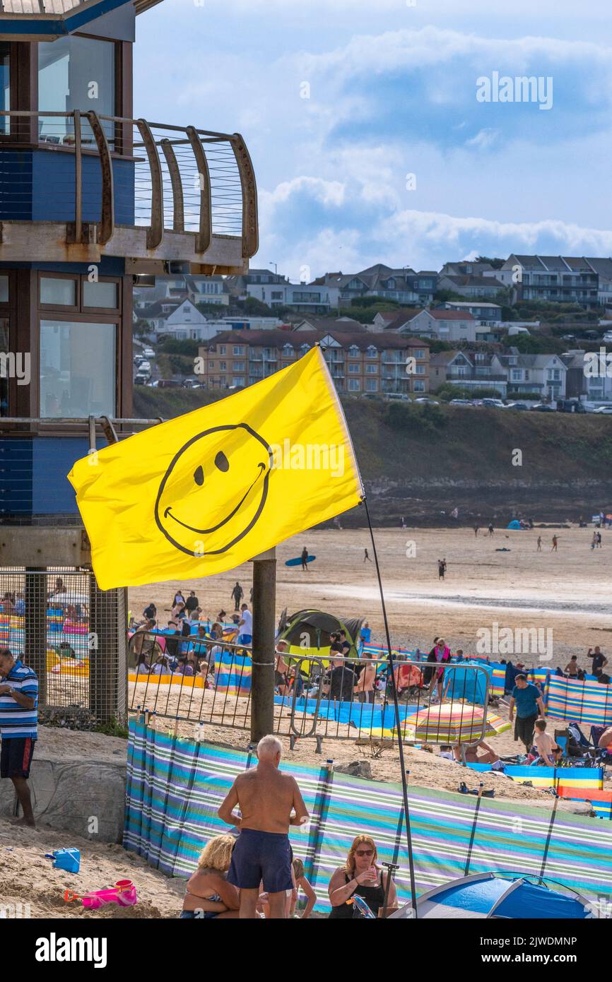 A flag with a smiley face symbol fluttering on a busy crowded Fistral ...