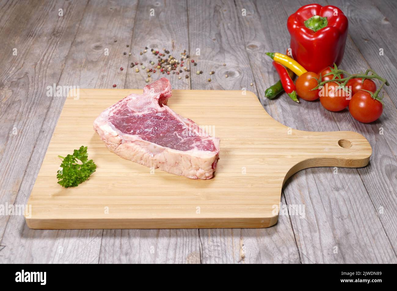 A fresh raw beef steak meat on a wooden board and vegetables on a table ...