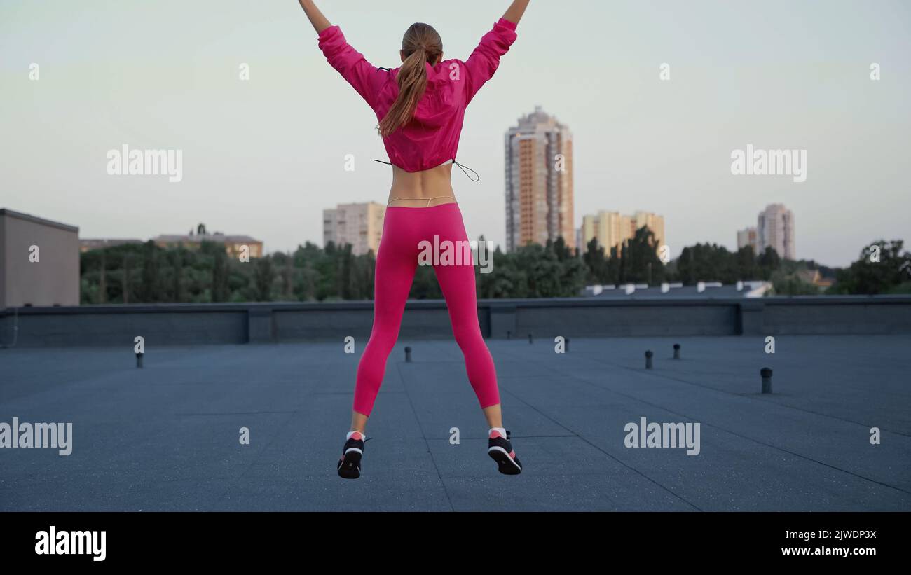 Back view of sportswoman jumping on roof of building in evening,stock ...