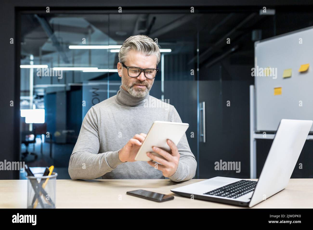 Senior experienced gray haired man in glasses using tablet computer ...