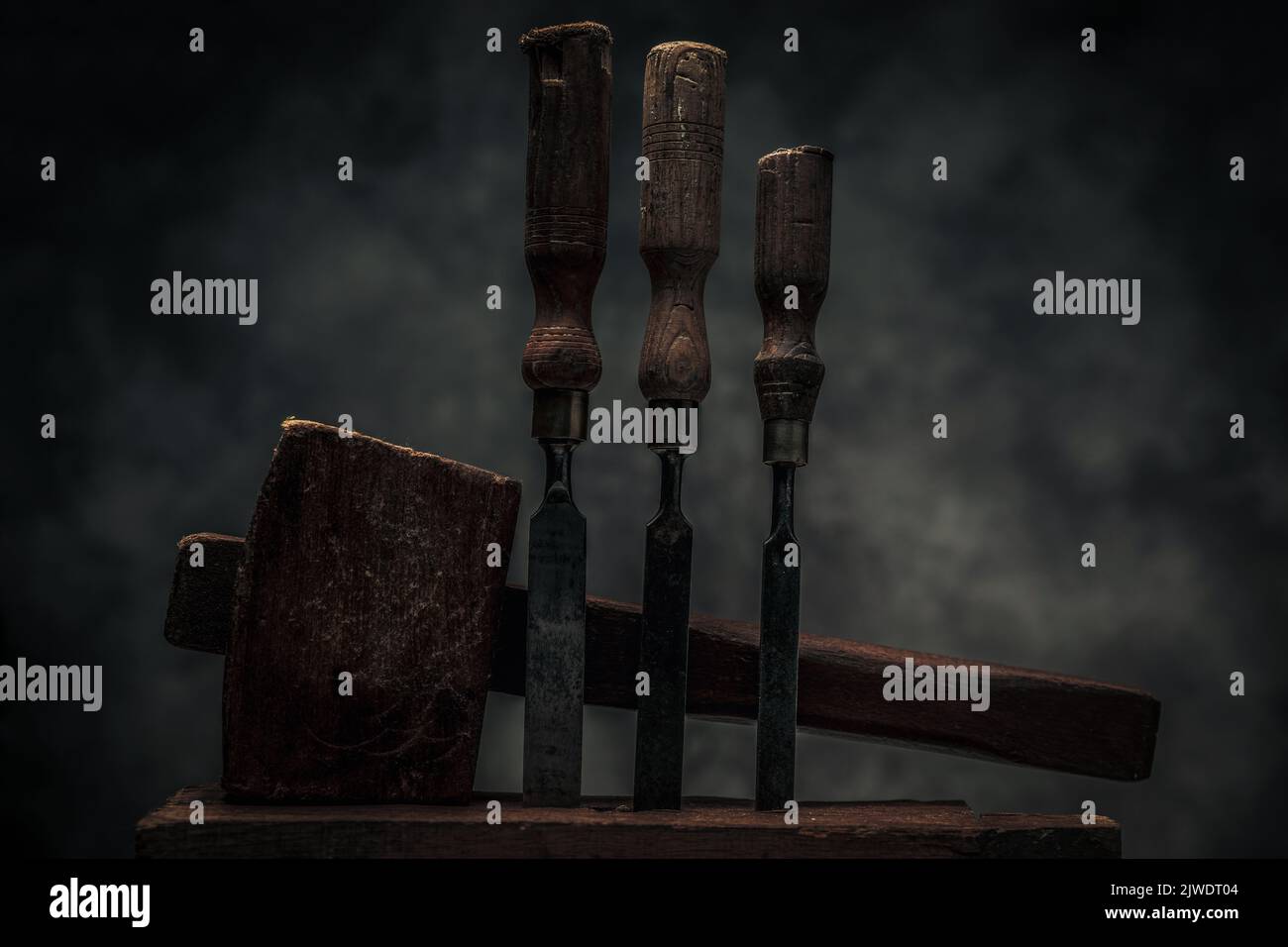 collection of old rusty carbon steel chisels with carving hammer behind in front of dark texture ...