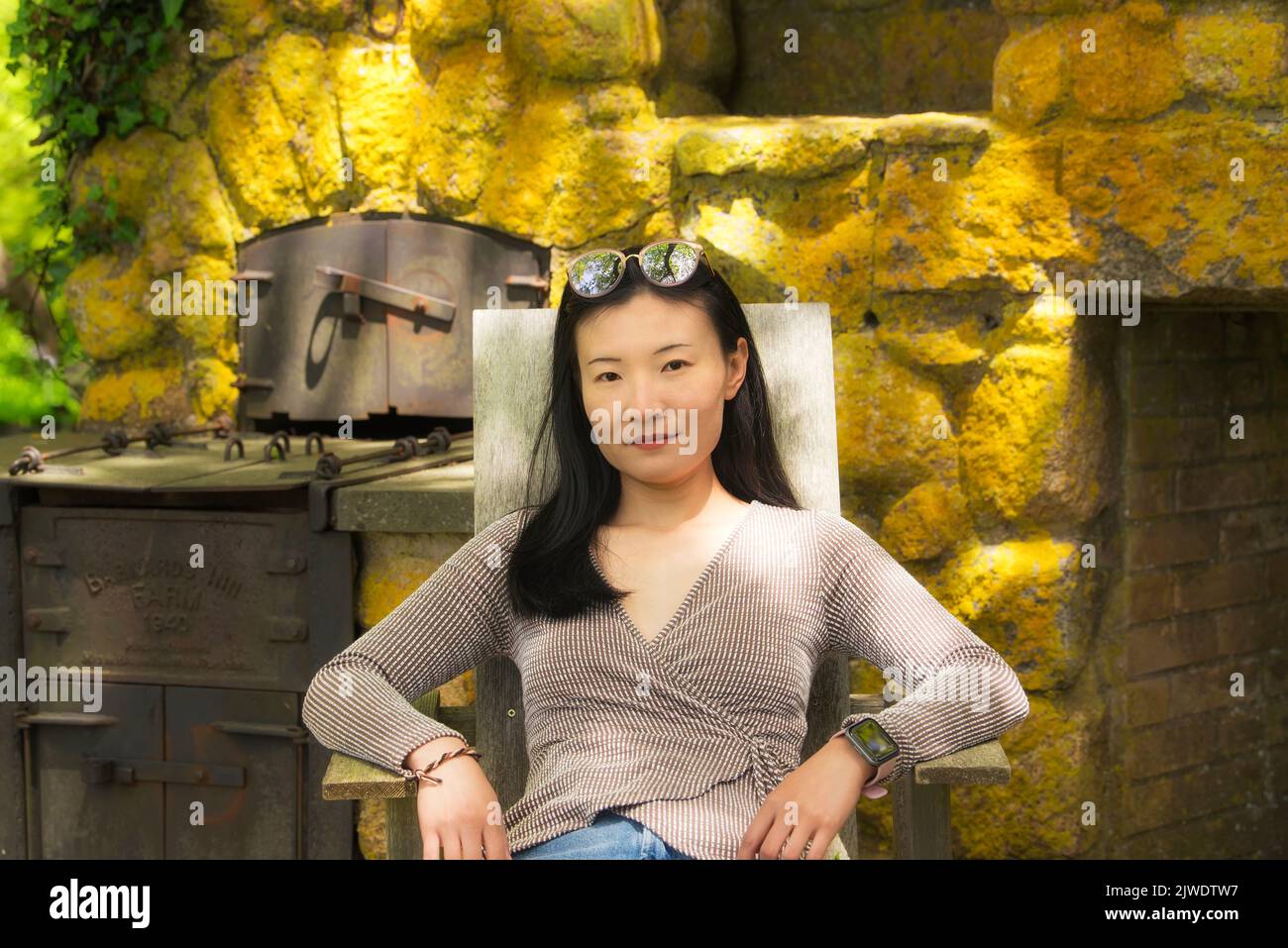 A Happy Chinese Woman Sitting In Front Of A Yellow Stone Outside Oven