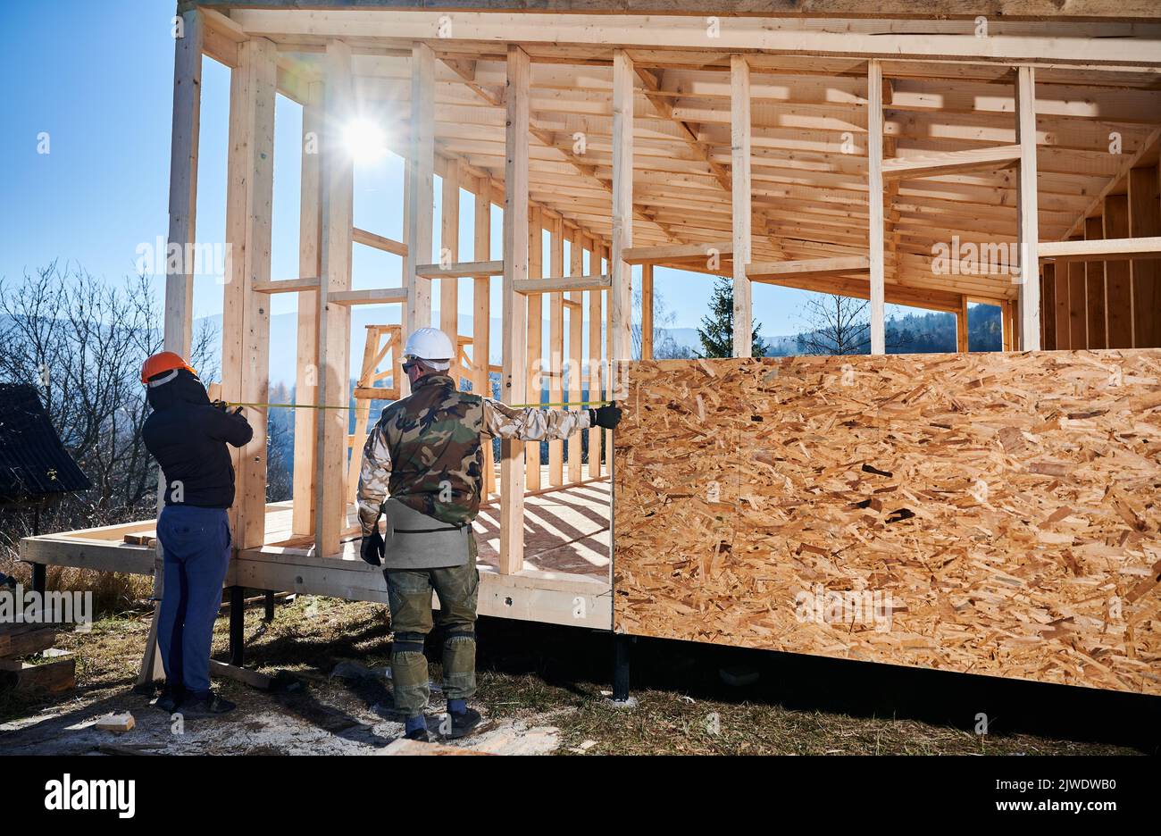 Men workers building wooden frame house on pile foundation. Back view ...