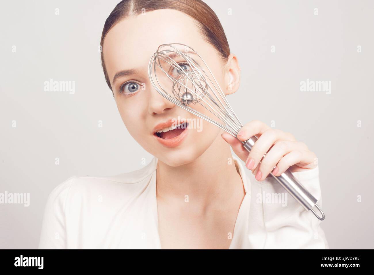 The girl chef holds a whisk and poses with him on a white background ...